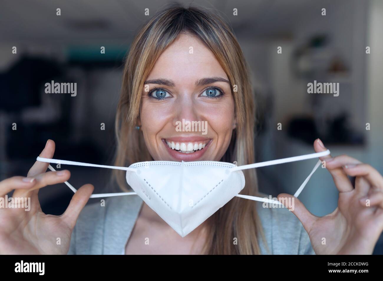 Portrait of smiling young woman putting on protective mask Stock Photo ...