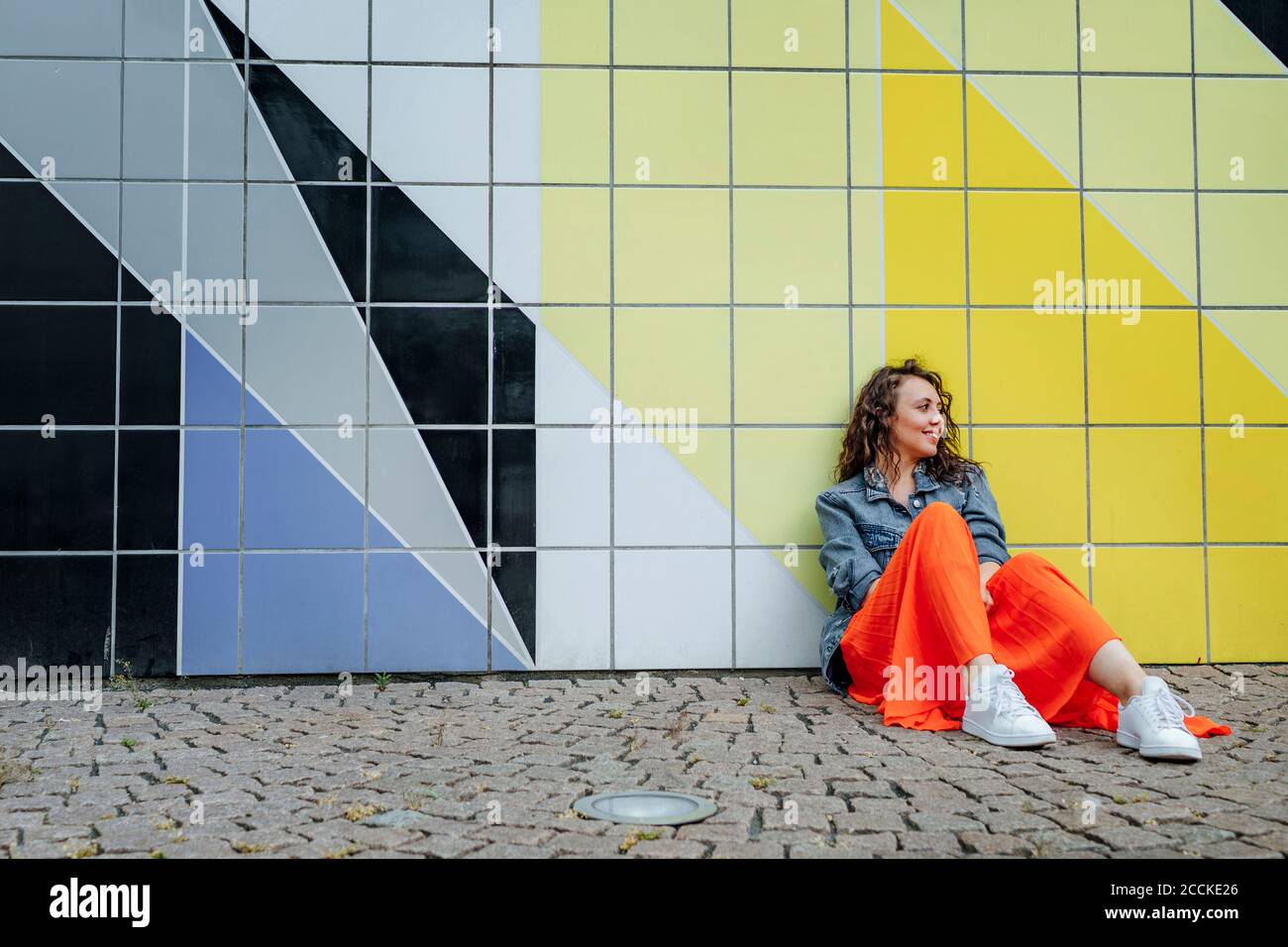 Young woman sitting on the ground in city, leaning on tiled wall Stock ...