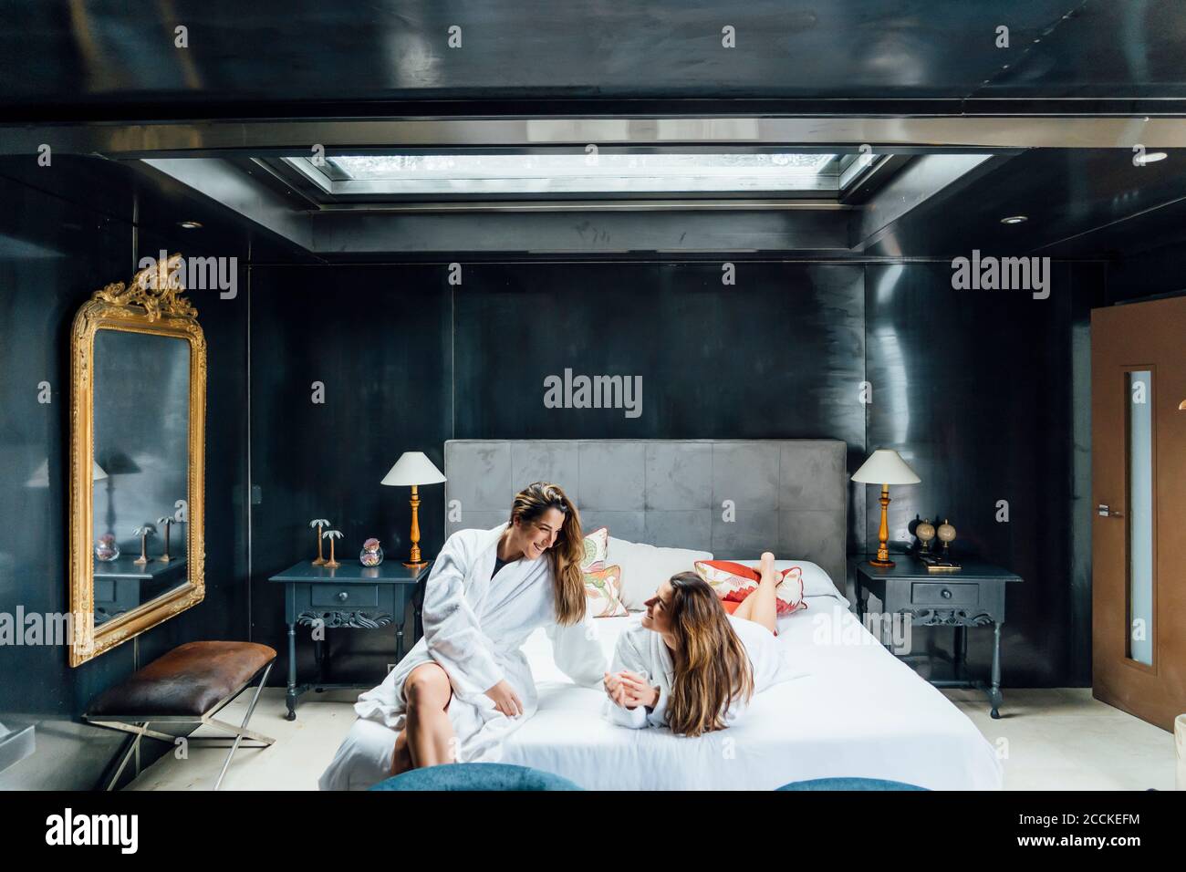 Twin sisters talking while relaxing on bed in hotel room Stock Photo ...