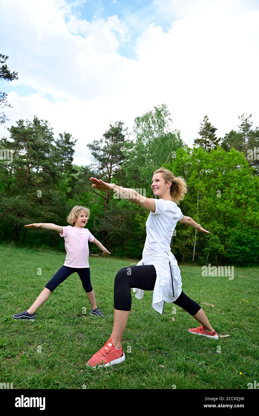 Happy mother and daughter practicing warrior 2 position in forest Stock ...
