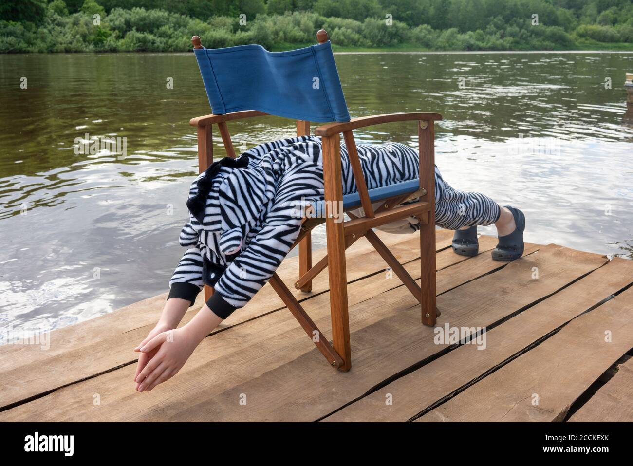 Boy in zebra costume exercising on chair by lake Stock Photo - Alamy