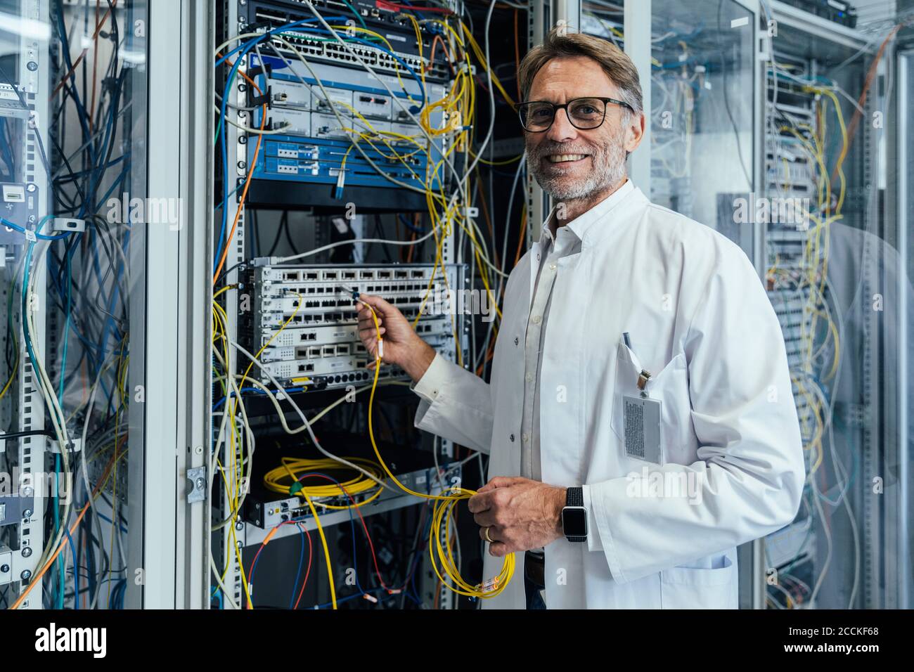 Smiling mature man plugging transceiver on fiber optic cable in data ...
