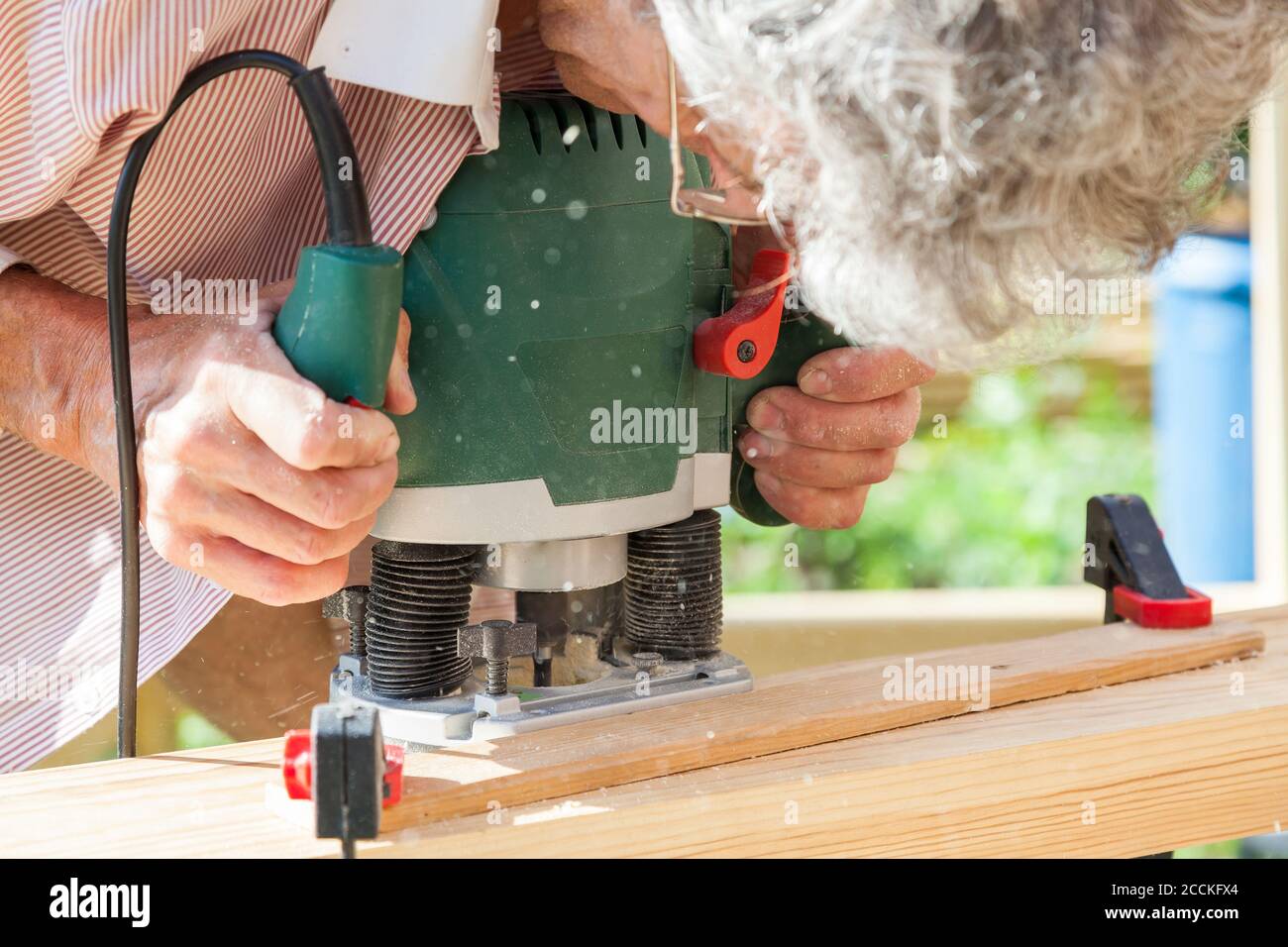 A man with gray hair carpenter bent over a green milling machine ...