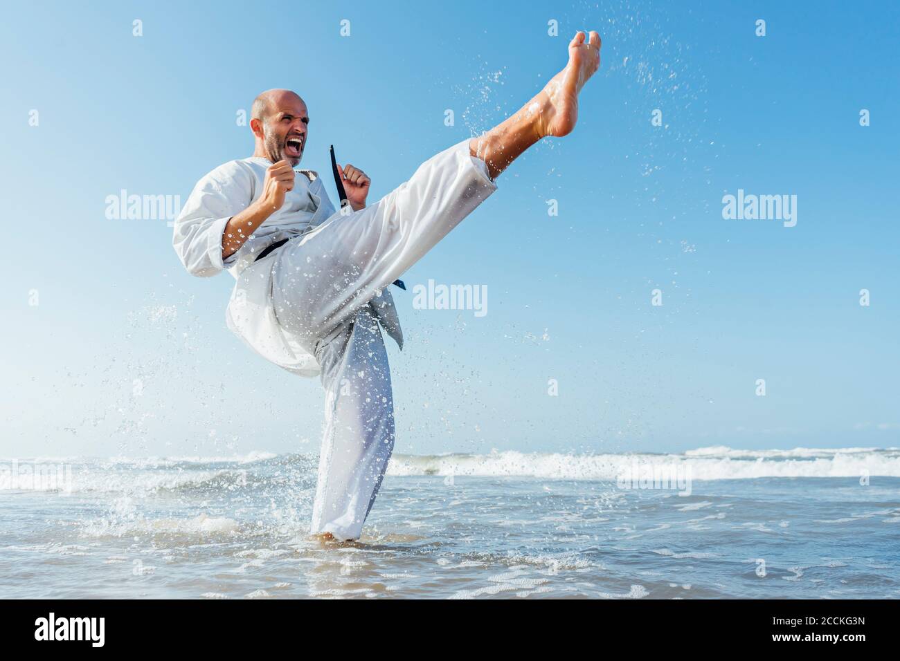 Mature man screaming while practicing karate in sea against clear sky ...