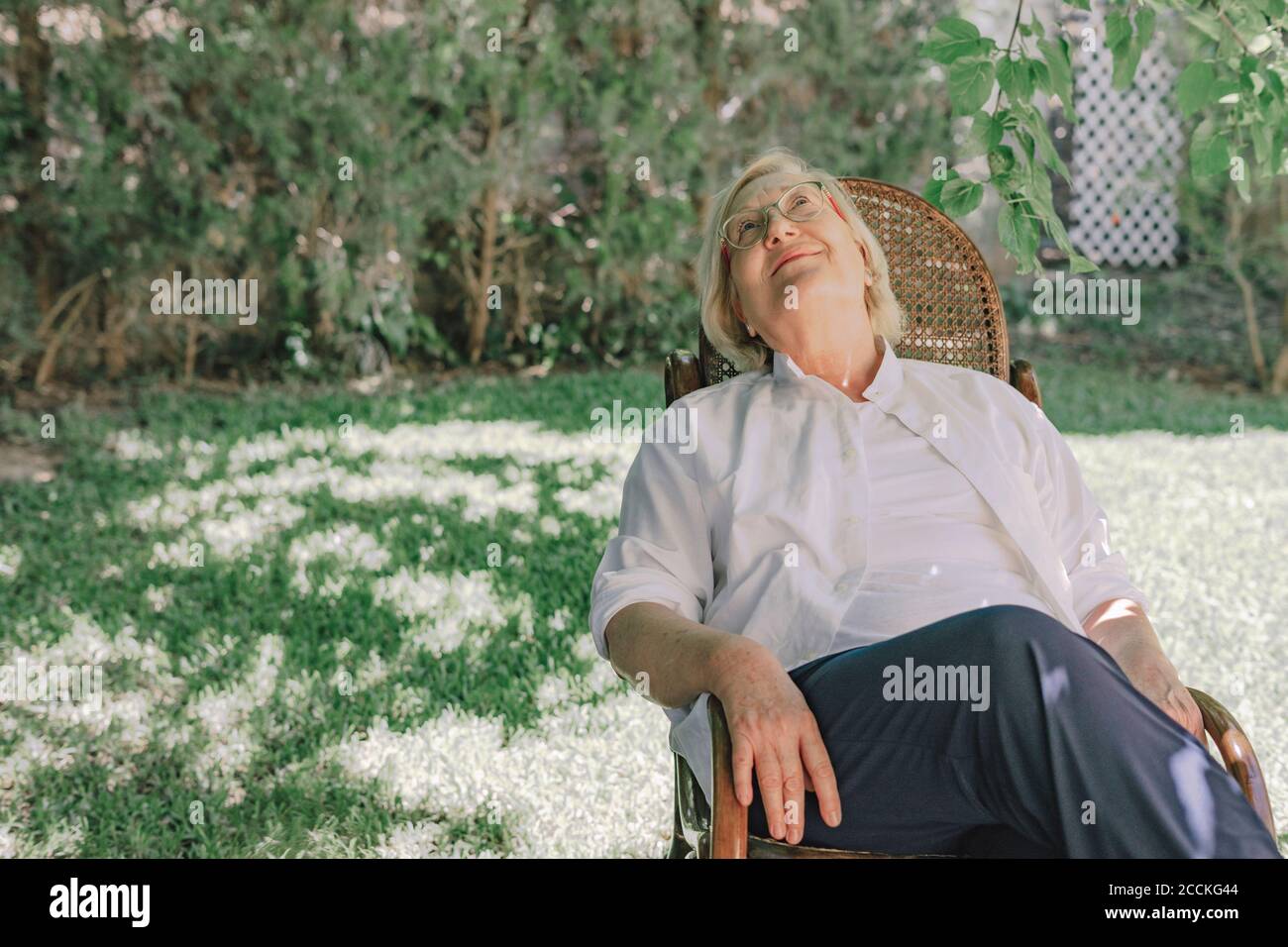 Thoughtful Senior Woman Looking Up While Relaxing On Chair In Yard