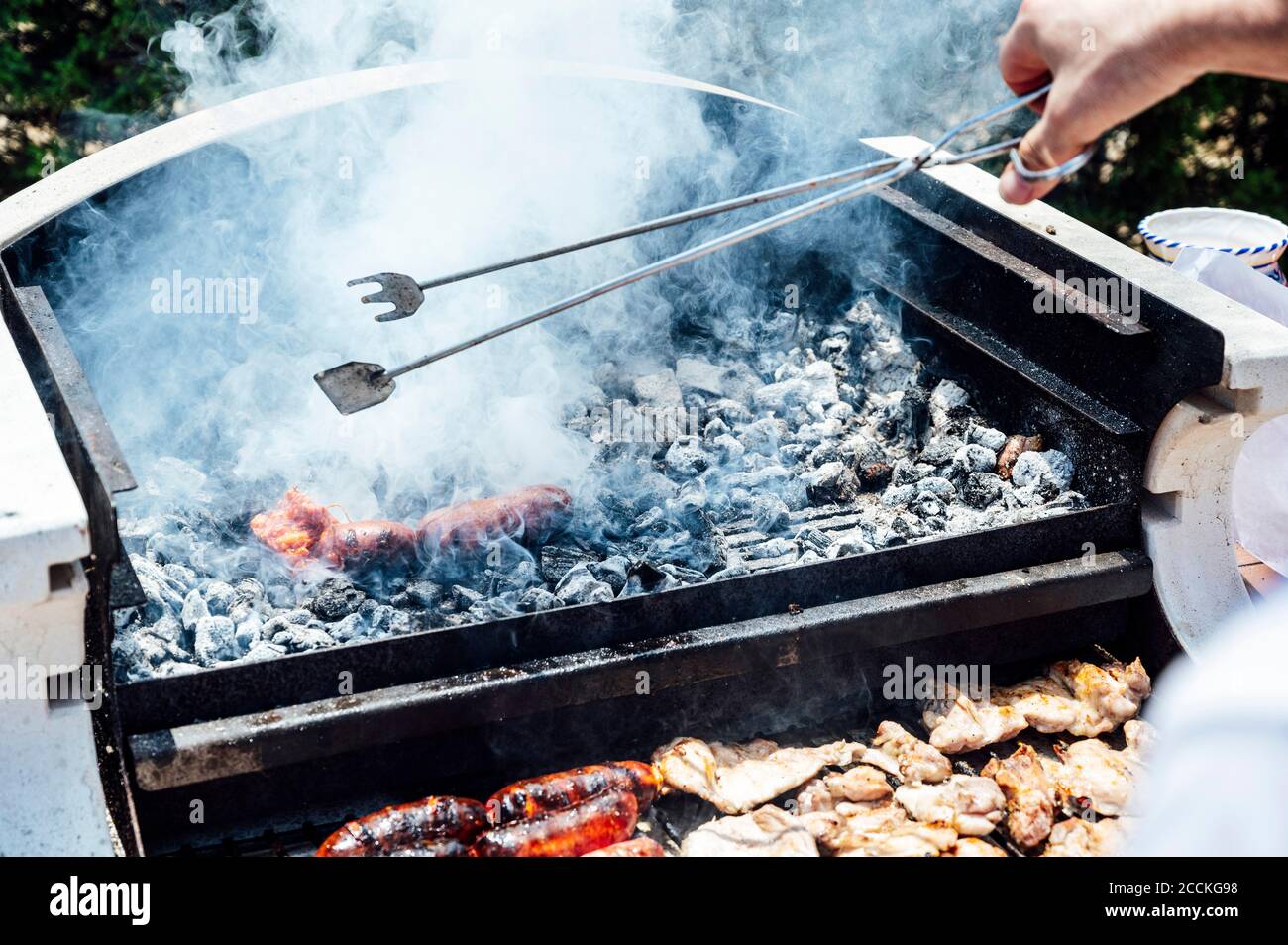 Hand of young man holding serving tongs over barbecue grill in yard ...