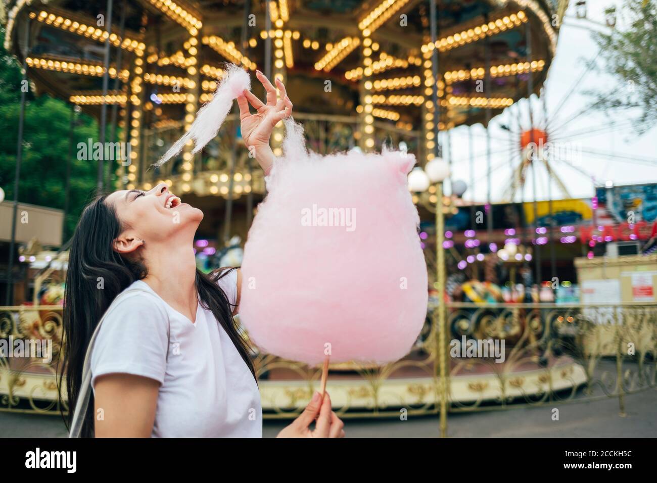 Happy beautiful woman eating cotton candy while standing against ...