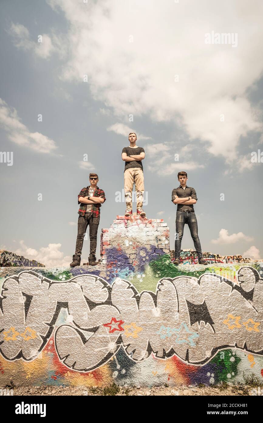 Teenage friends standing on a graffiti wall in an old run down ...