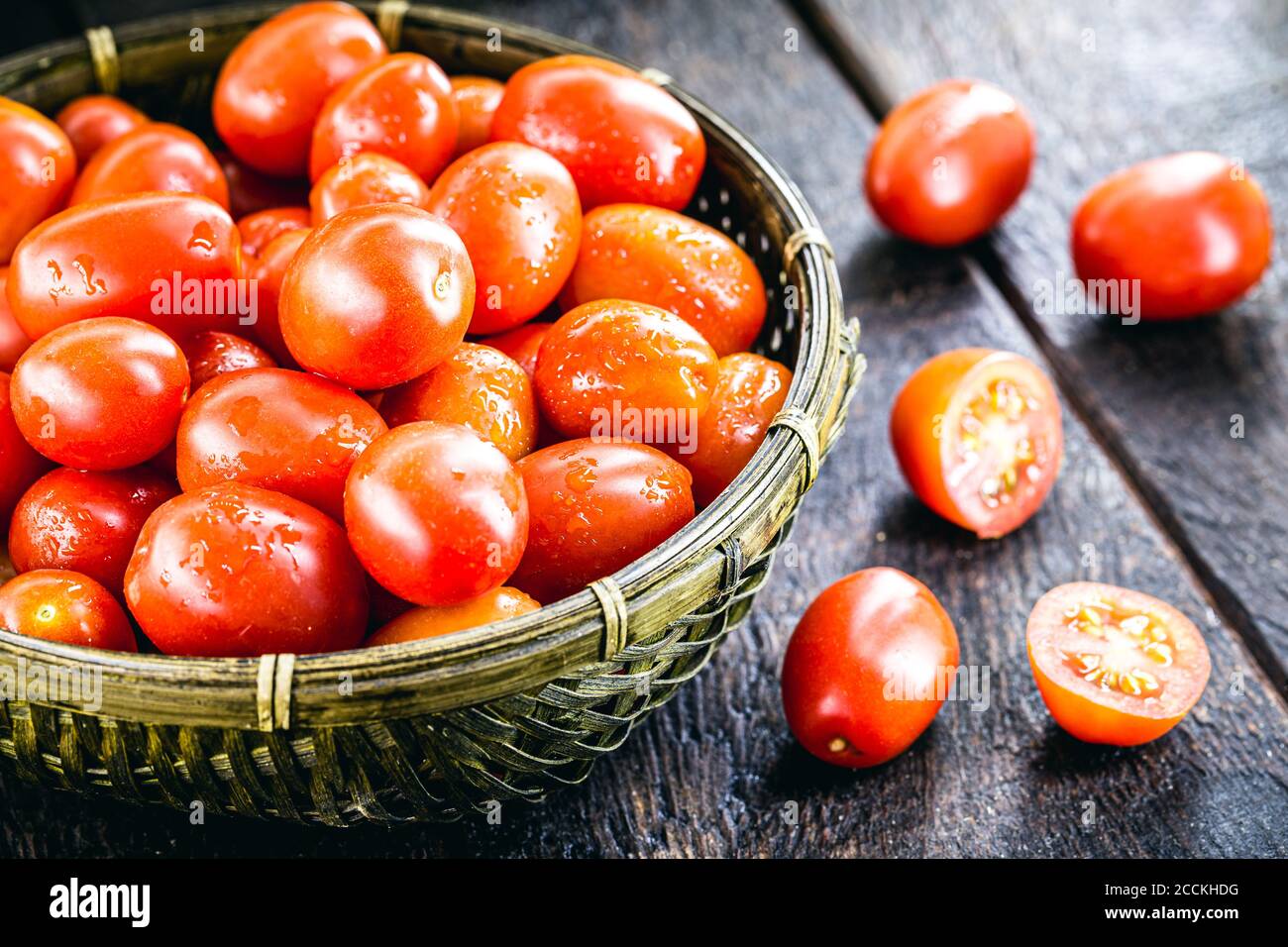 small tomato, vibrant red, fruit in a rustic straw basket. Sweet tomato ...