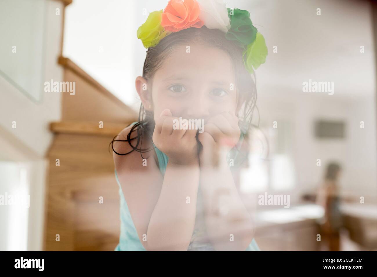 Close-up of cute girl wearing colorful tiara looking through glass at ...