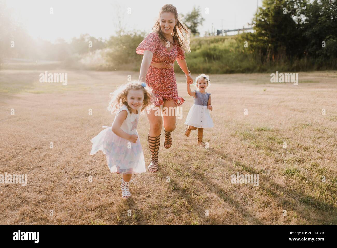 Happy mother running with daughters on a meadow in backlight Stock ...