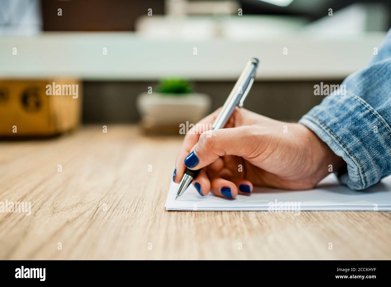 Businesswoman's hand writing on document at wooden desk in modern ...