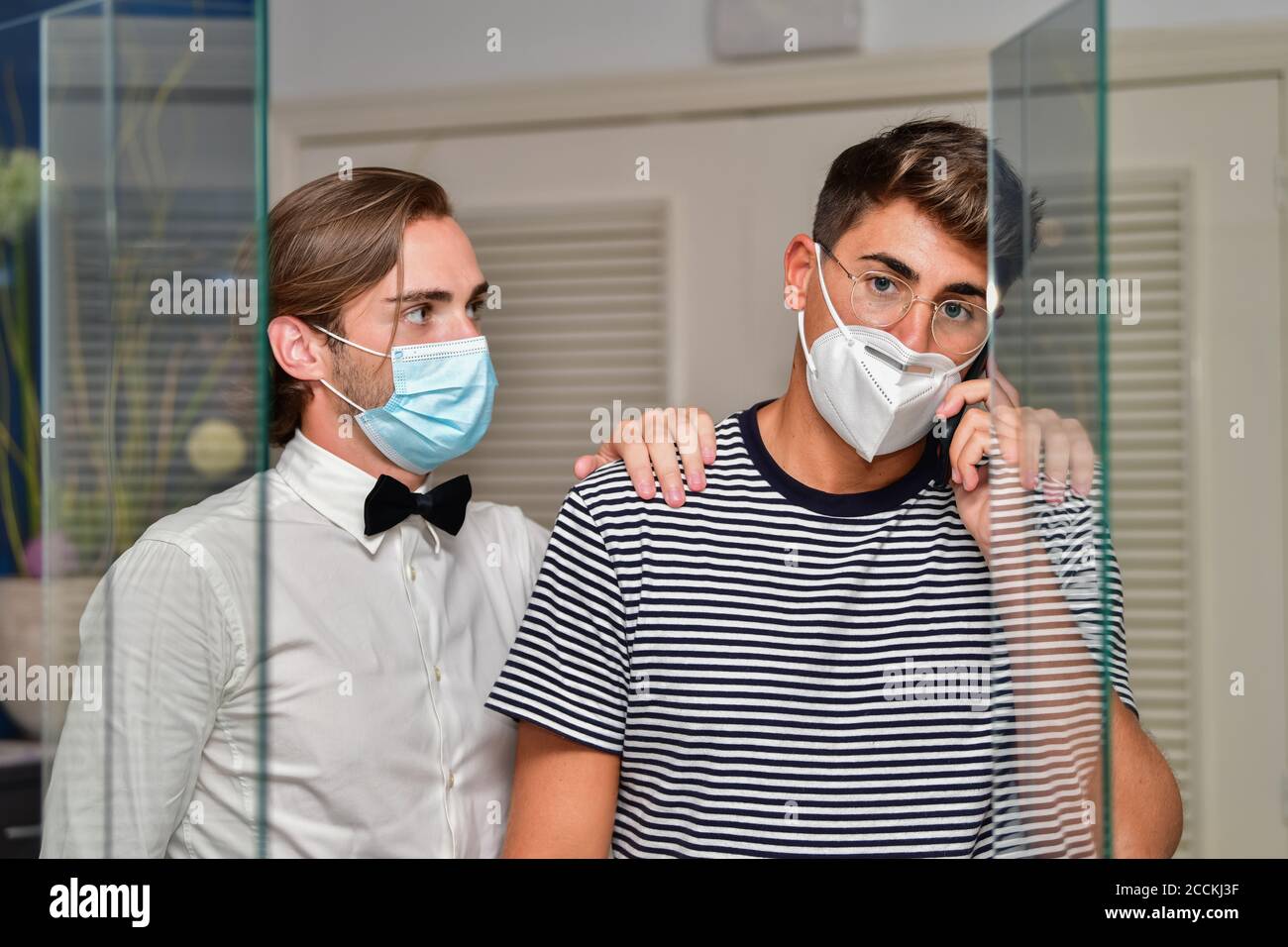 Young man wearing a surgical mask puts his hand on the shoulder of ...