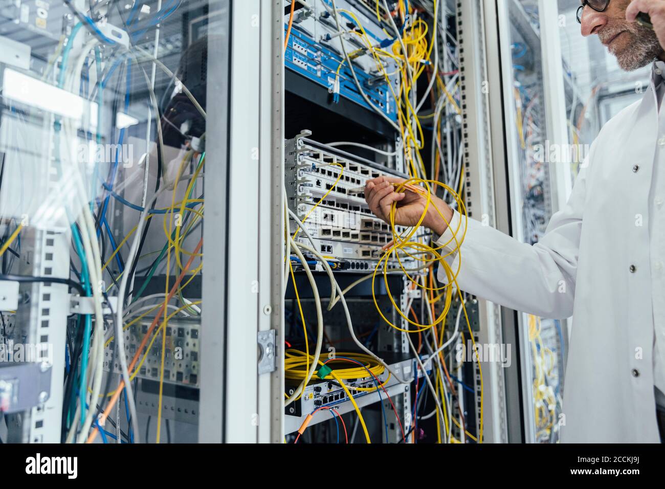 Mature man plugging in transceiver on fiber optic cable in data center ...