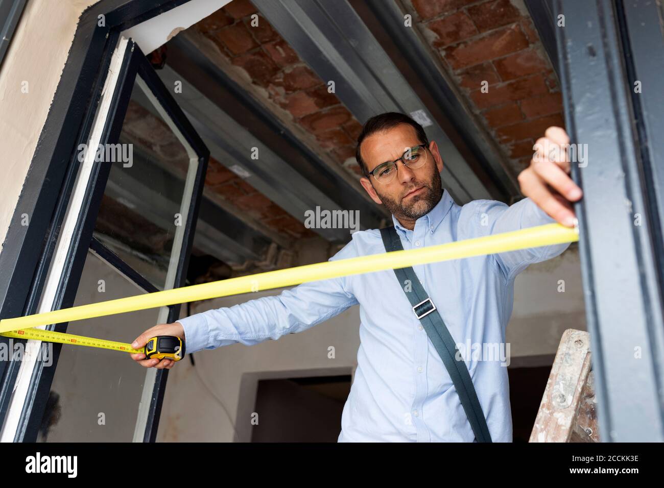 Architect using tape measure on window frame in a house under ...