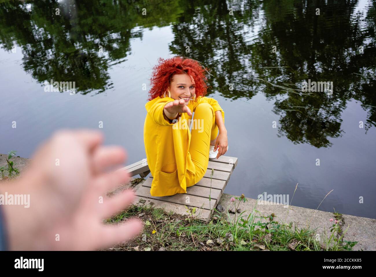 Young woman with curly hair and yellow suit sitting by the riverside ...