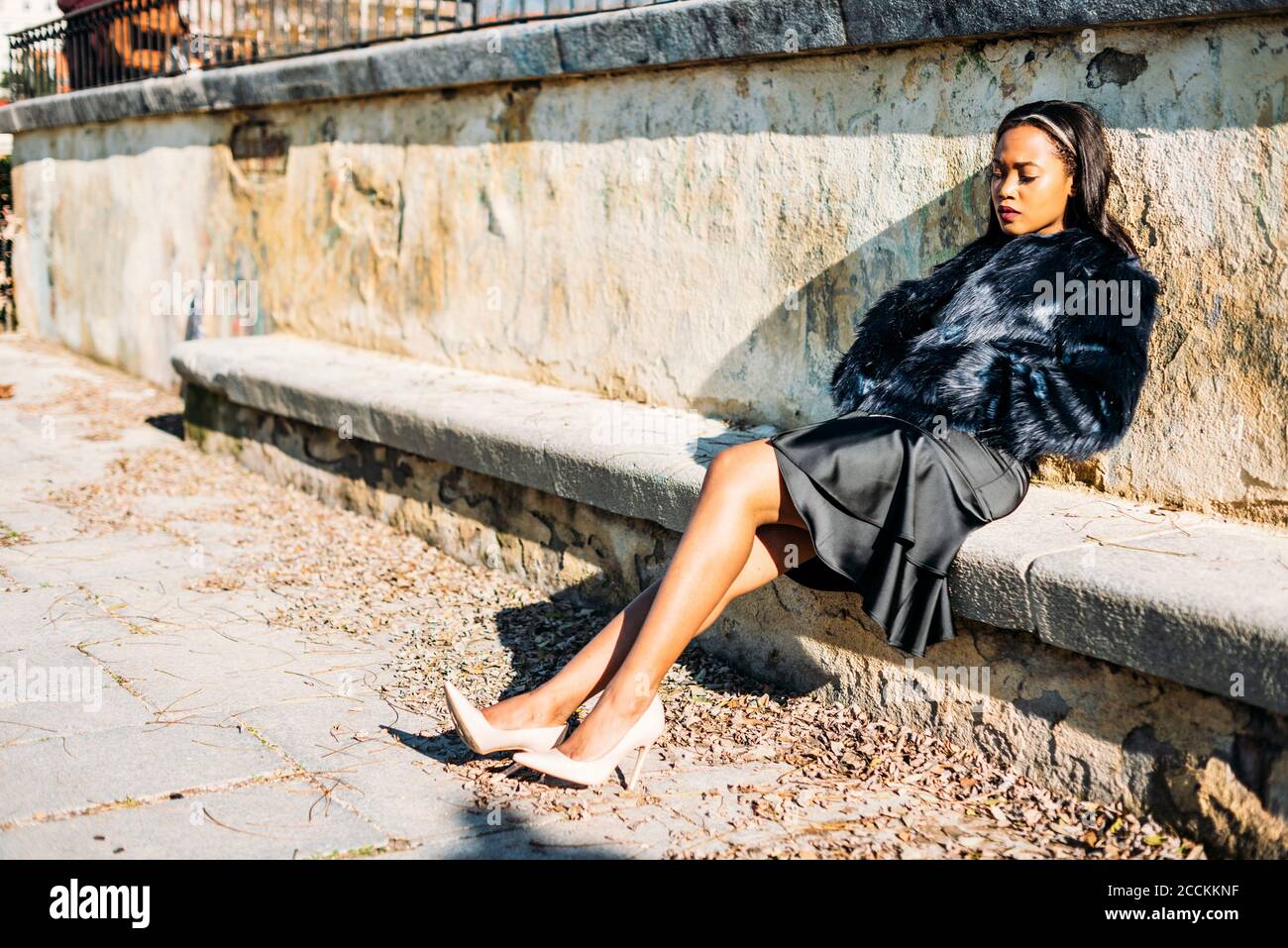 Beautiful young woman sitting on bench and leaning on wall Stock Photo ...