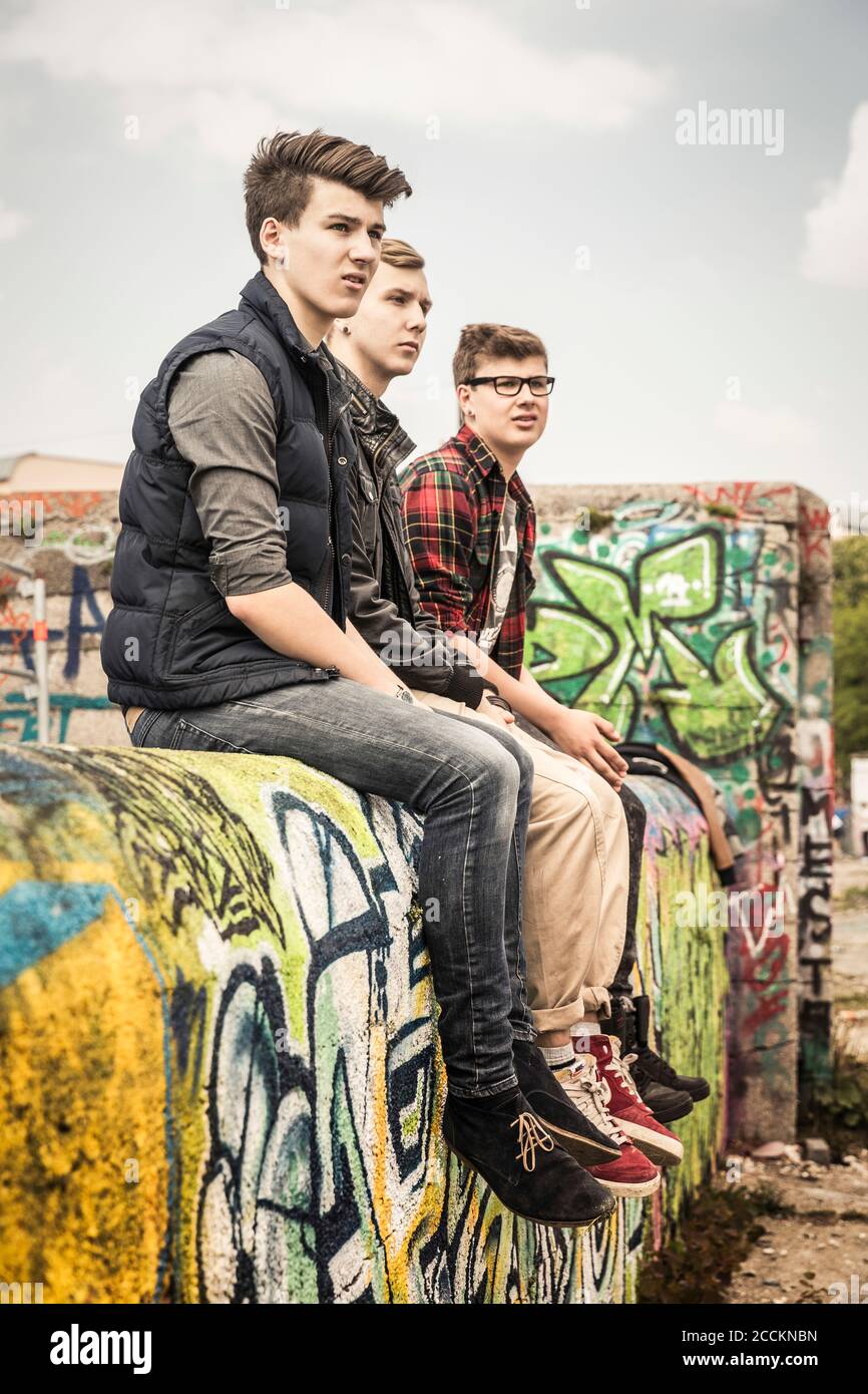 Group of friends sitting on a graffiti wall in an old run down ...