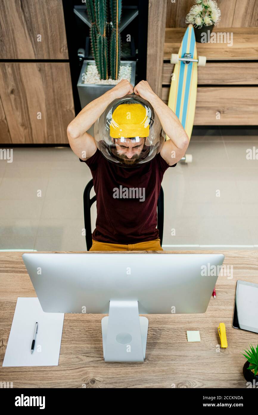 Tensed businessman wearing fishbowl while using computer in modern ...