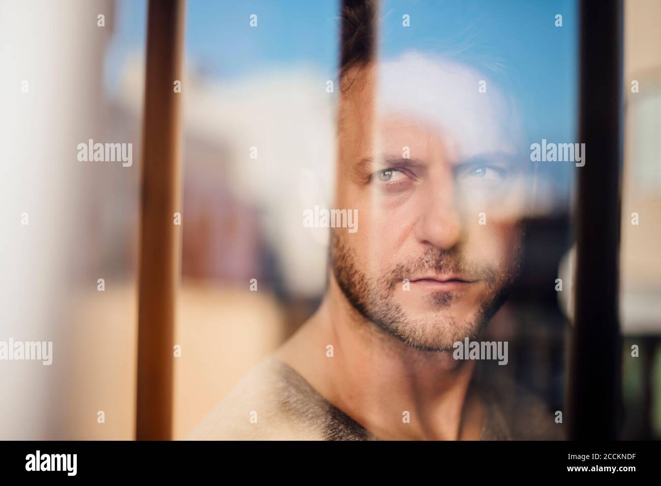Close-up of thoughtful man looking through window seen through glass ...