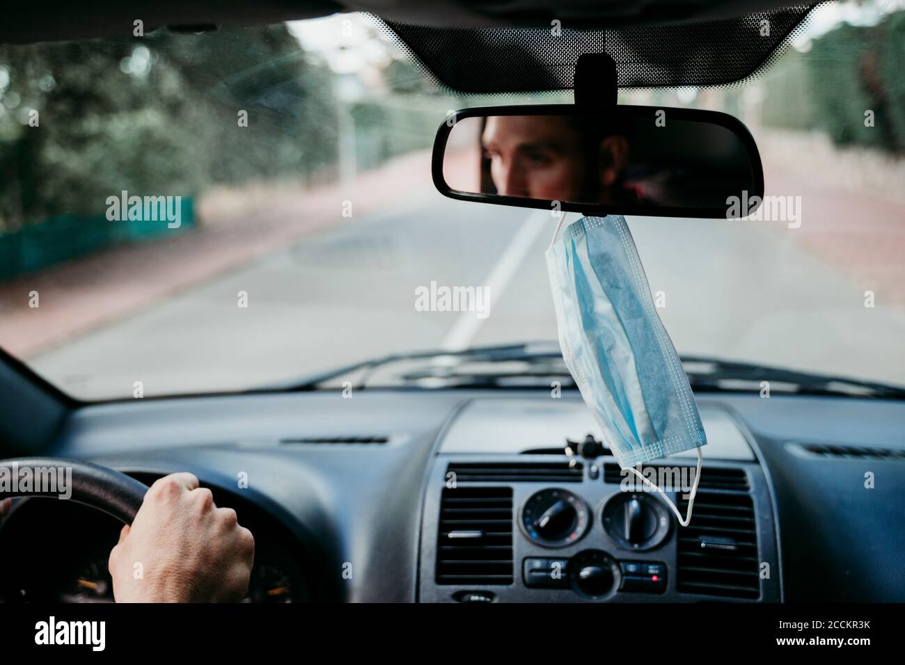 Close-up of protective face mask hanging on rear-view mirror in car ...