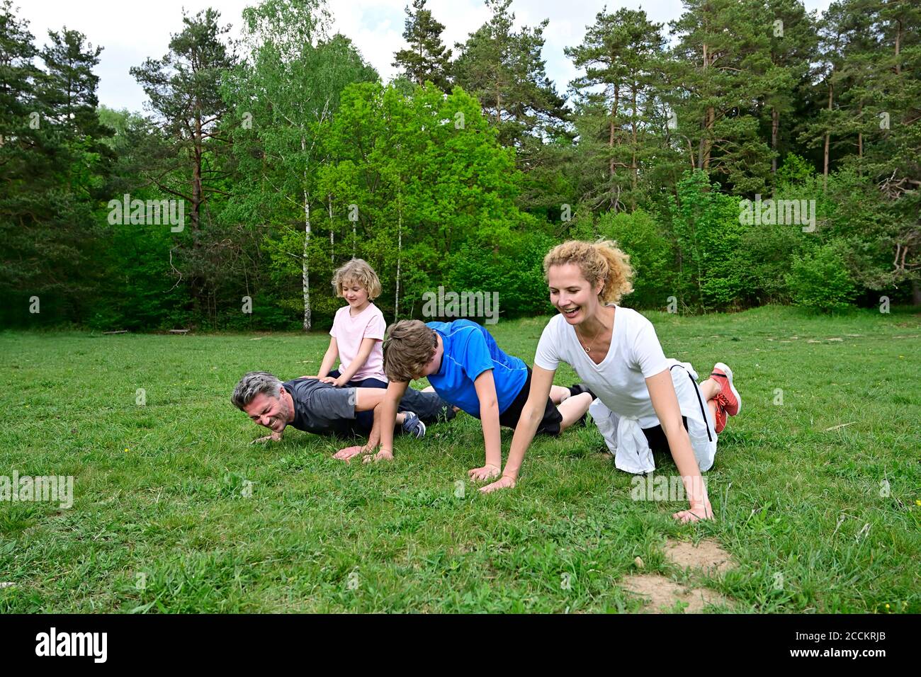 Family doing push-ups on grassy land against trees in forest Stock ...