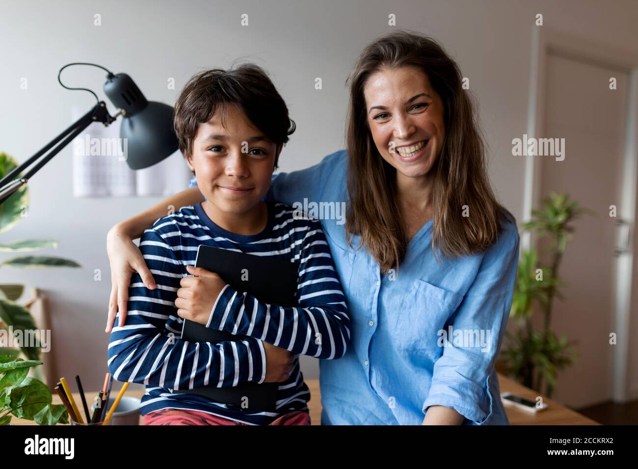 Smiling female tutor with hand on boy's shoulder sitting at home Stock ...