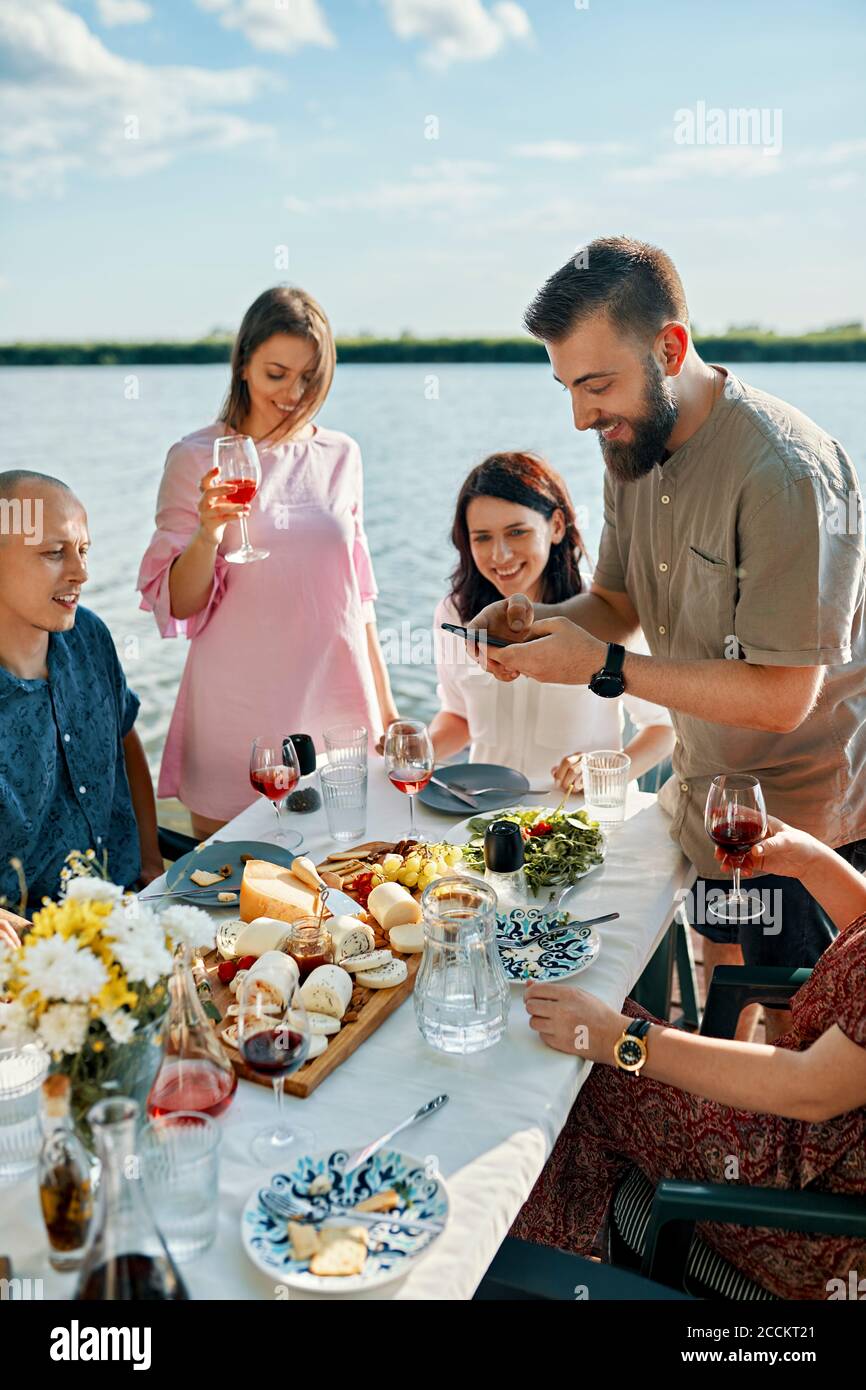 Friends having dinner at a lake taking smartphone picture Stock Photo ...