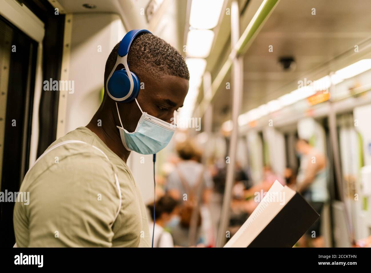 Close-up of young man wearing mask reading book and listening music ...
