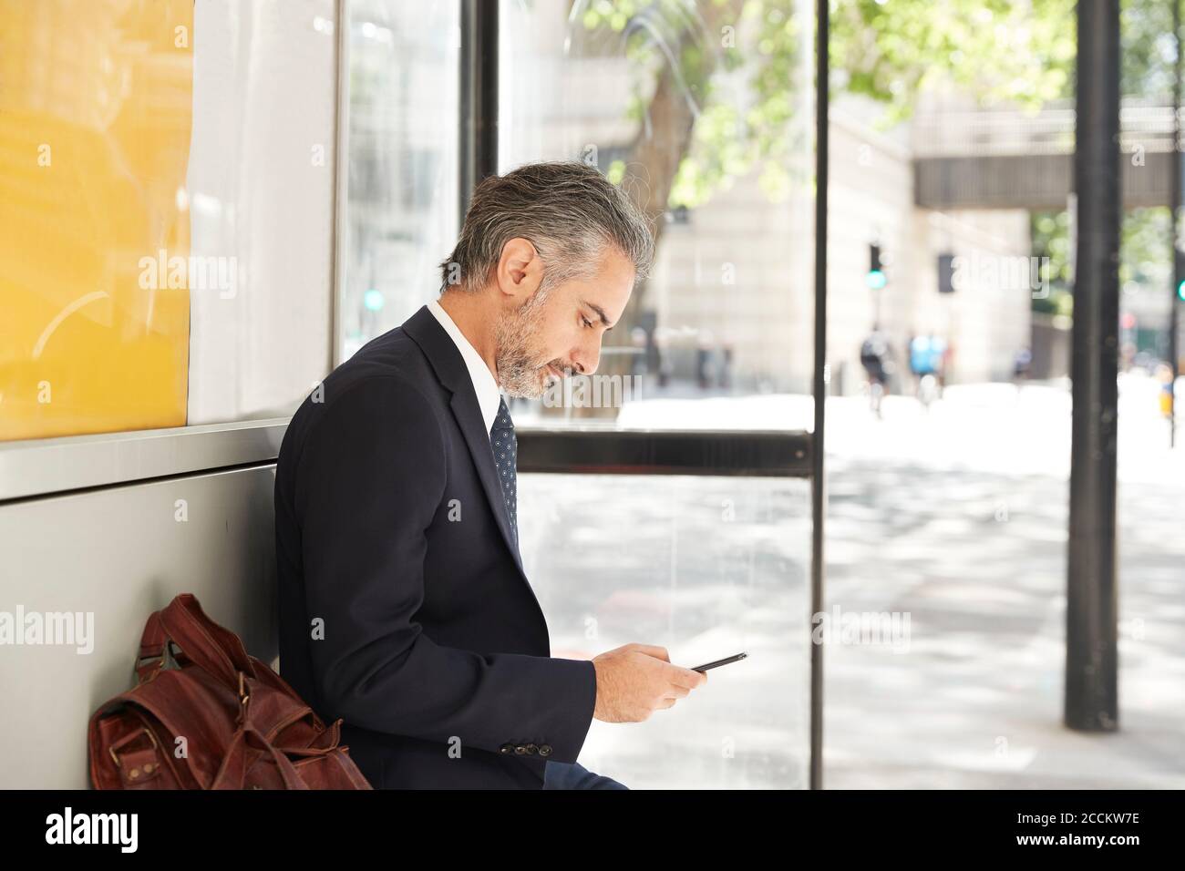 Businessman using phone while sitting at bus stop Stock Photo - Alamy