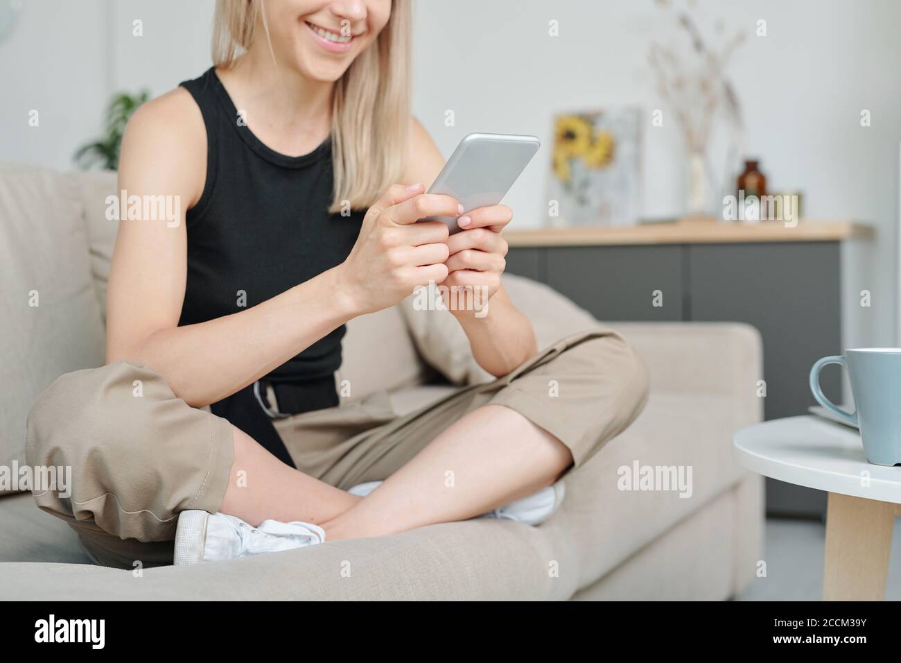 Happy female millennial sitting on couch with her legs crossed and ...