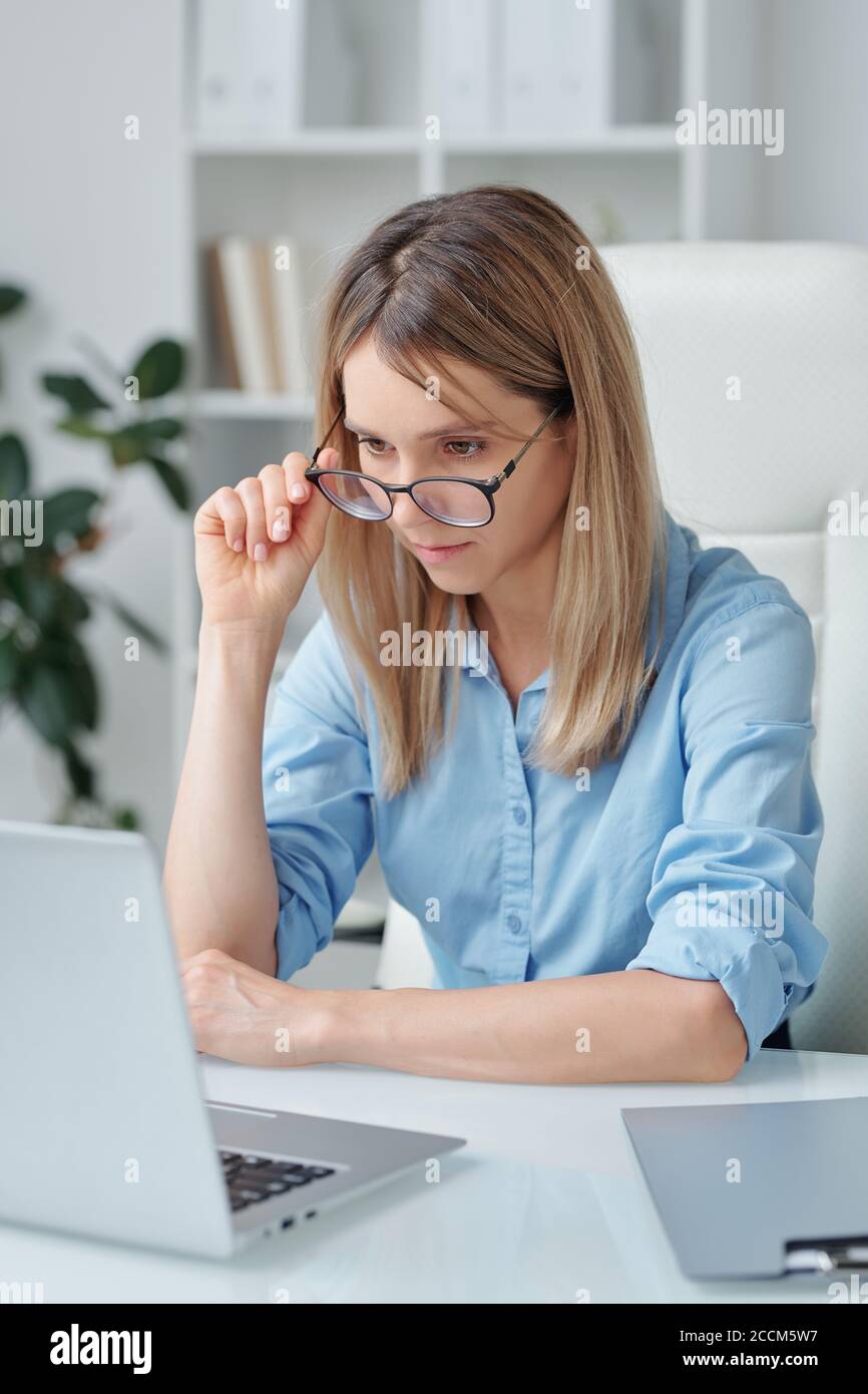 Blond pretty confident businesswoman in blue shirt looking at data on ...