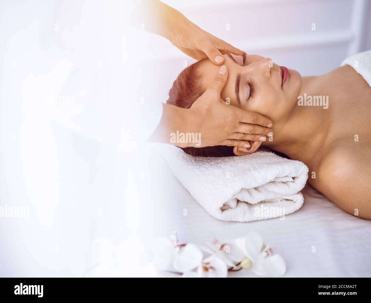 Beautiful brunette woman enjoying facial massage with closed eyes in ...