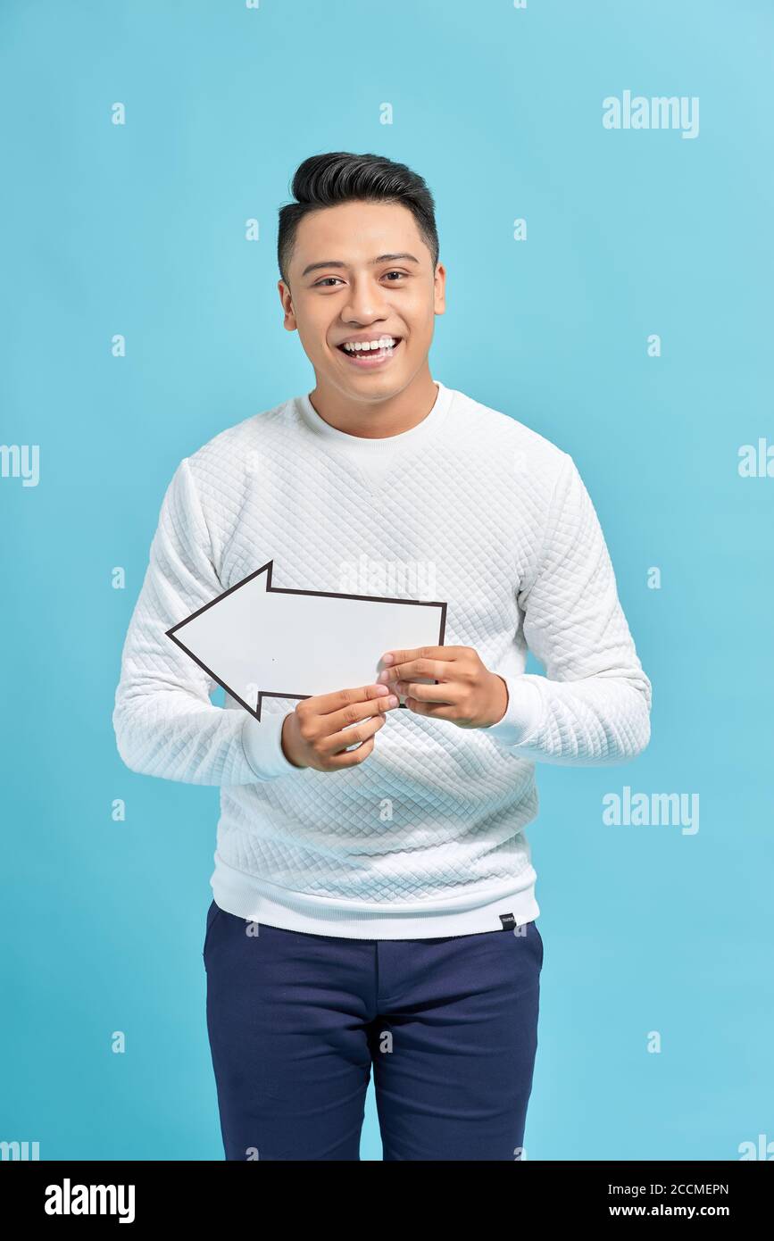 Happy smiling young man holding white thick upwards arrow pointing to ...
