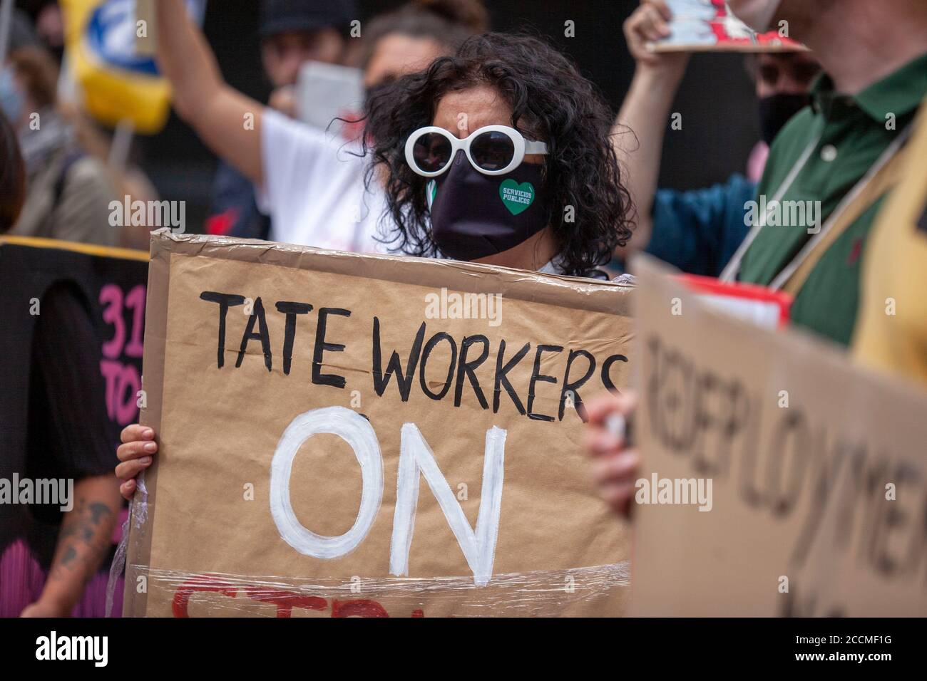 Female protester, wearing sunglasses and a face mask holding up a tate ...
