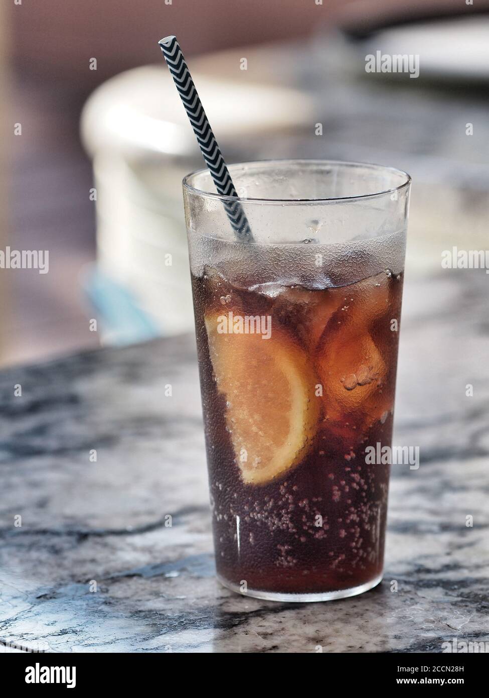 Glass of cola with ice cube, slice of lemon and straw in glass with ...