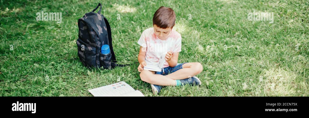 Elementary school boy sitting in park outdoor doing school homework ...