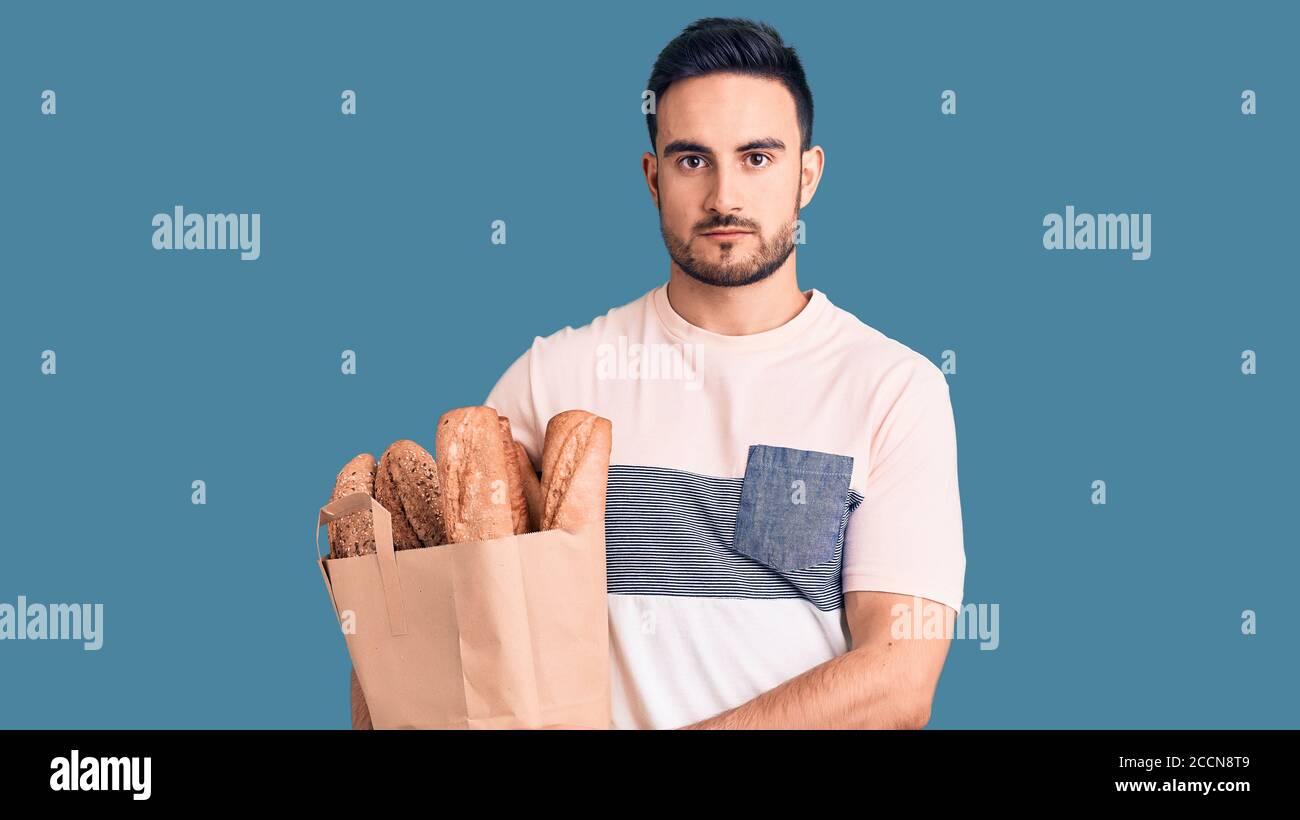 Young handsome man holding bread bag thinking attitude and sober ...