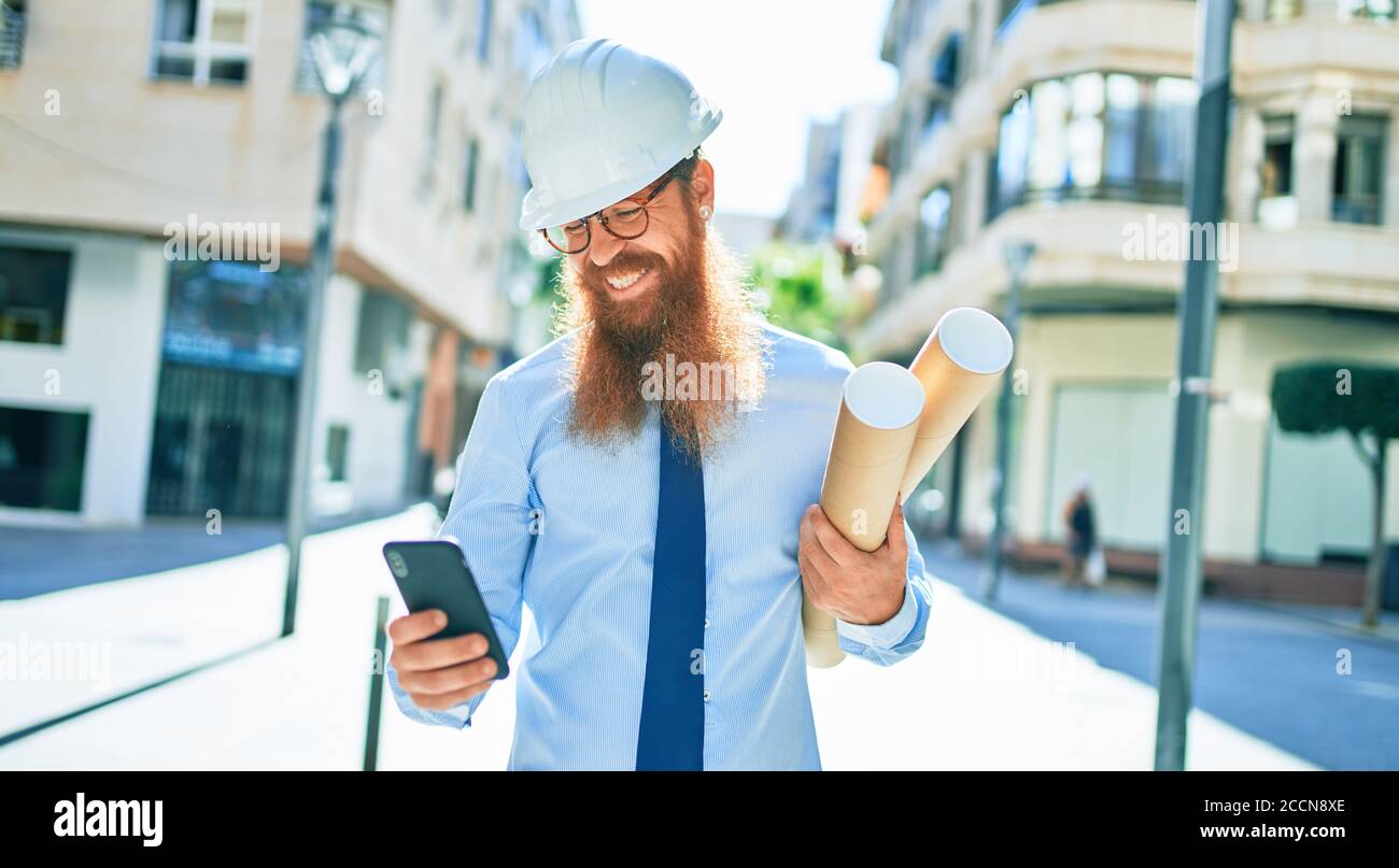 Young redhead architect man with long beard wearing hardhat smiling ...
