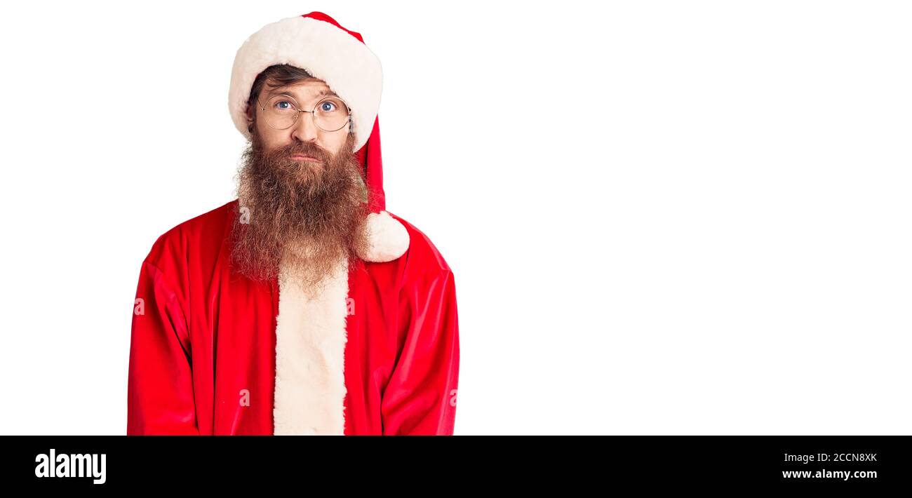 Handsome young red head man with long beard wearing santa claus costume ...