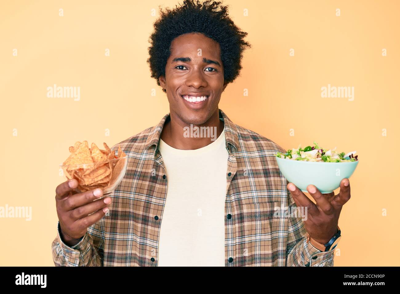 Handsome african american man with afro hair holding nachos and healthy ...