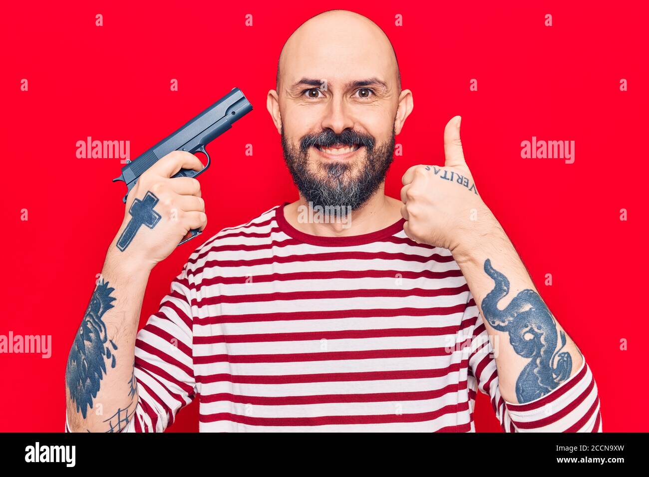 Young handsome man holding gun smiling happy and positive, thumb up ...