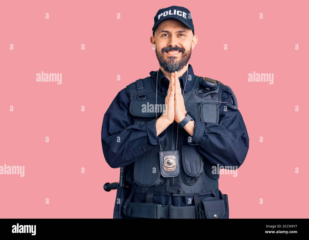 Young handsome man wearing police uniform praying with hands together ...