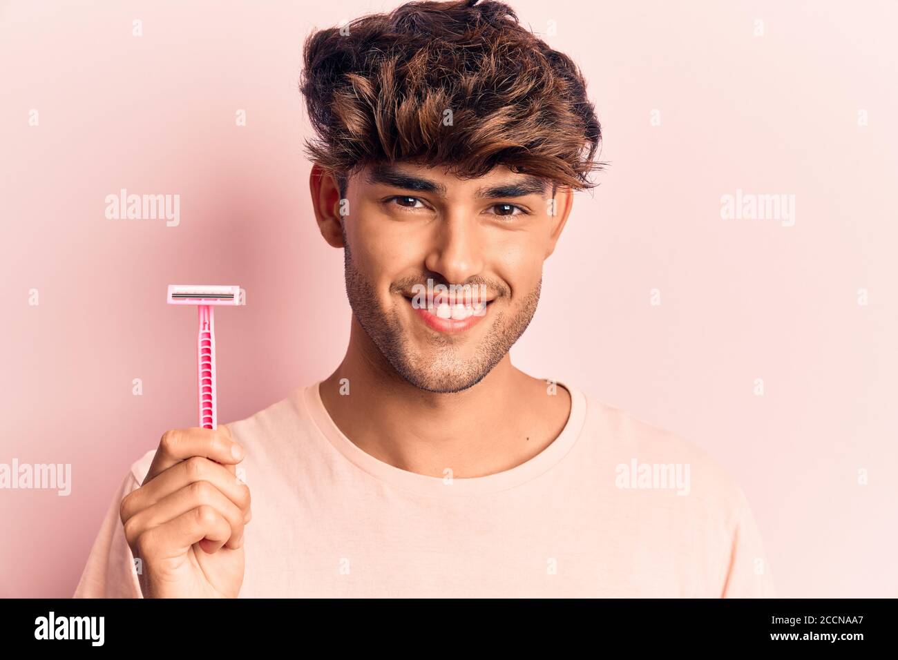 Young hispanic man holding razor looking positive and happy standing ...