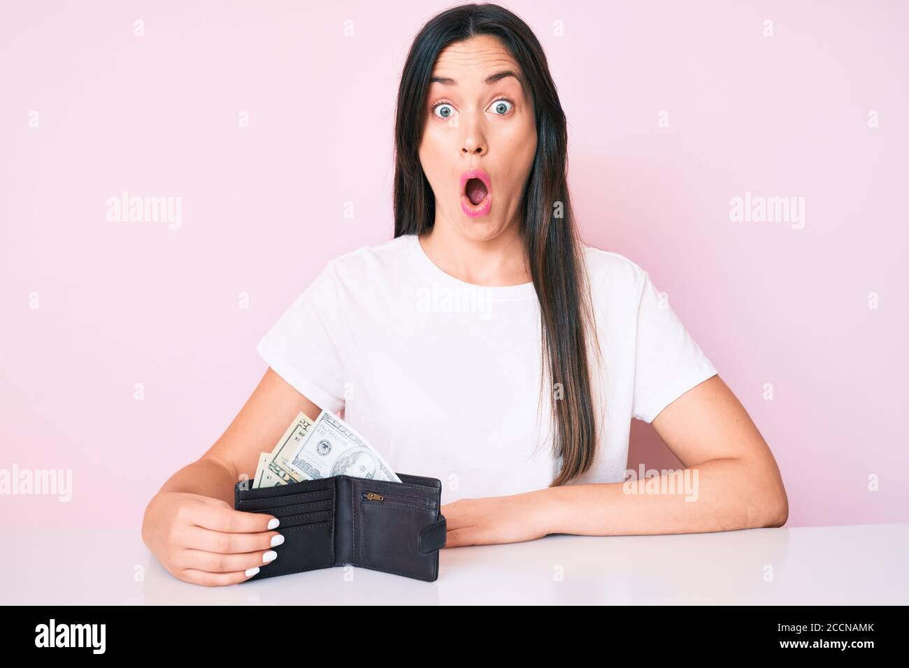 Young caucasian woman sitting at the table holding wallet with dollars ...