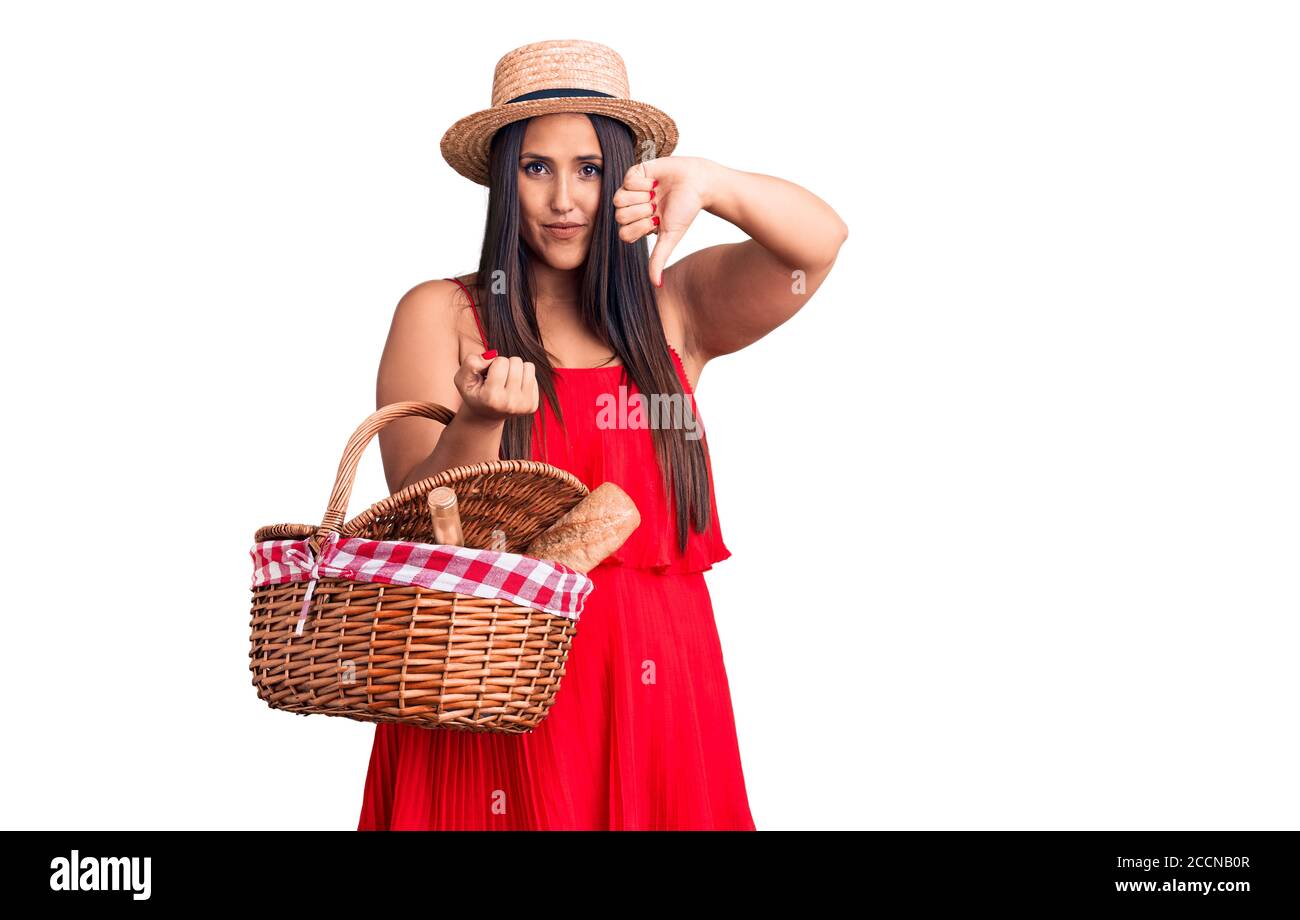 Young beautiful brunette woman wearing summer hat holding picnic basket ...