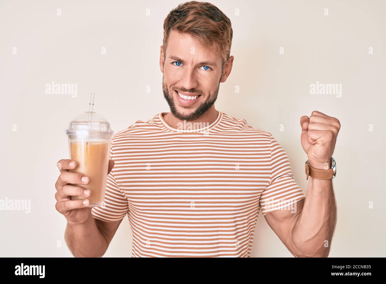 Young caucasian man drinking glass of orange juice screaming proud ...