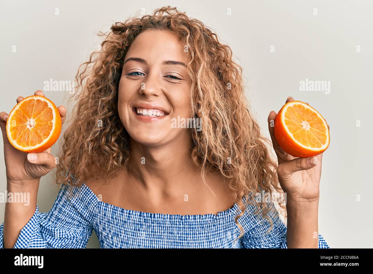Beautiful caucasian teenager girl holding fresh orange smiling and laughing hard out loud ...