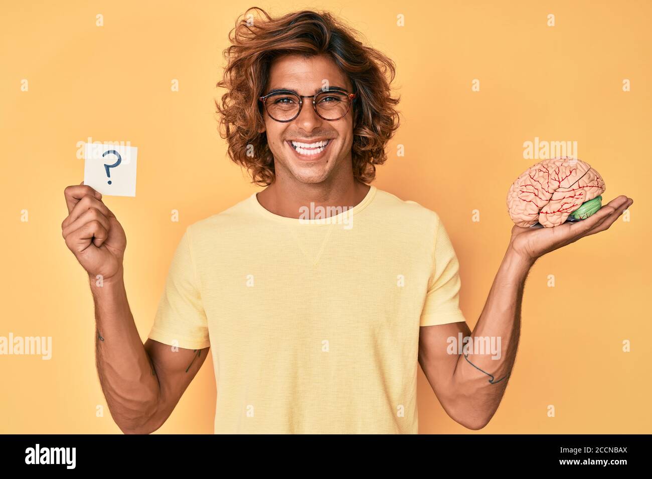 Young hispanic man holding brain and question mark smiling with a happy ...