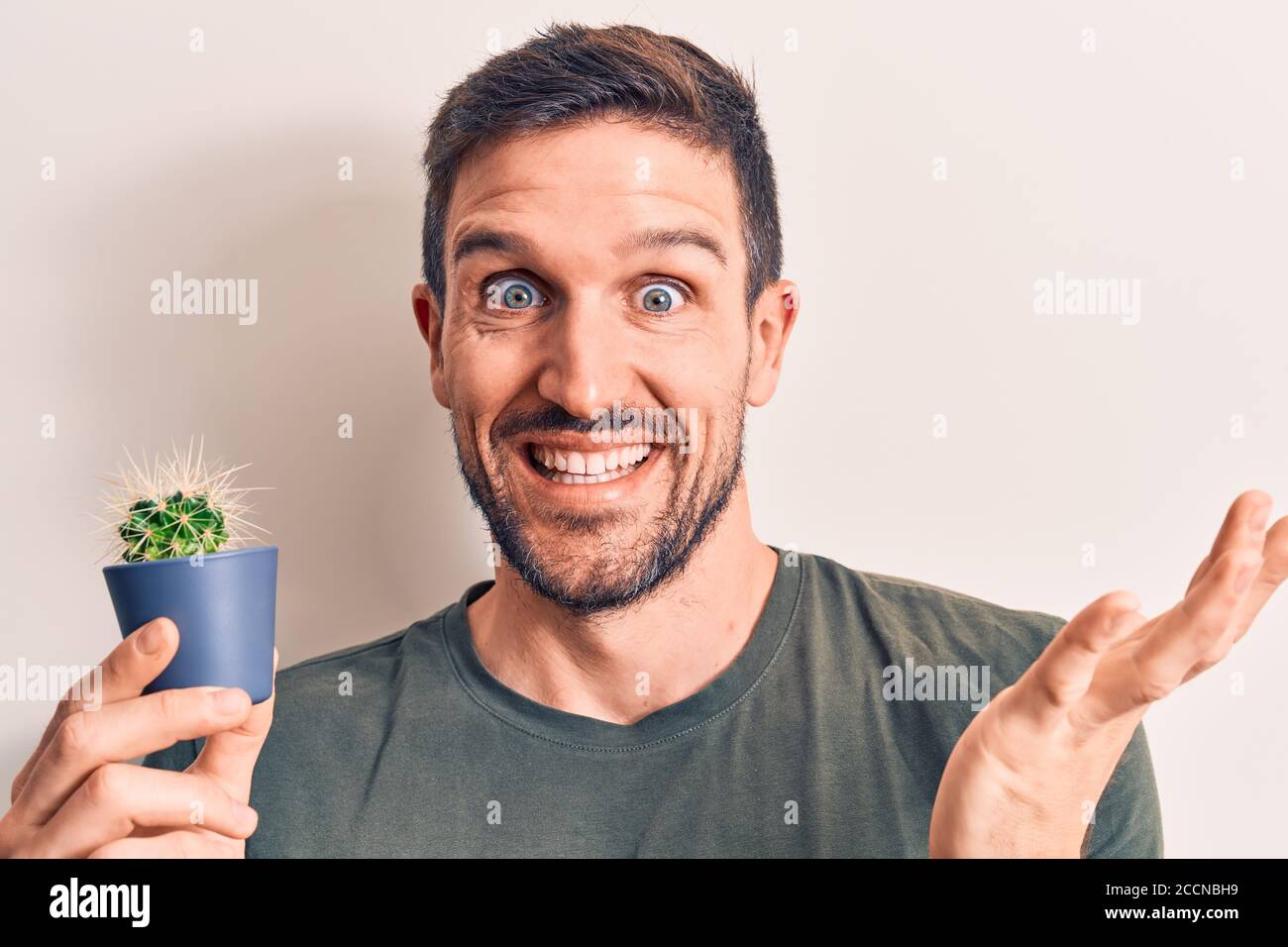 Young handsome man holding small cactus plant pot over isolated white ...